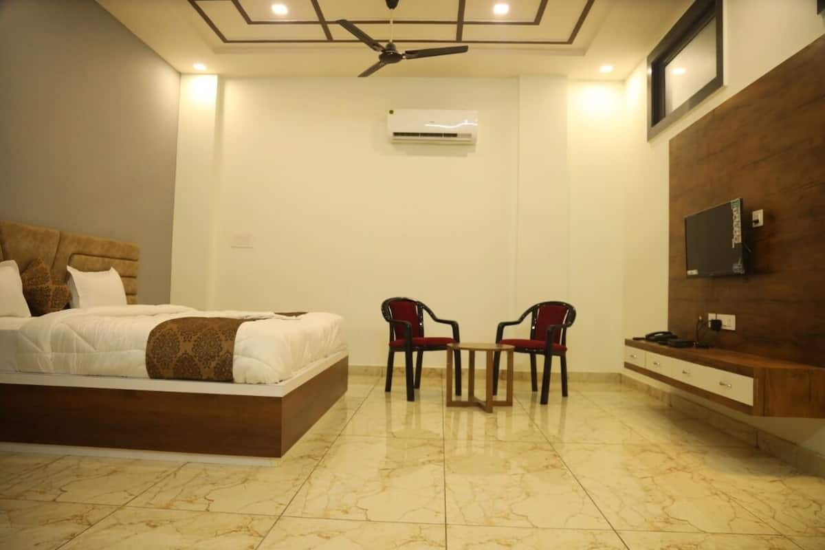 Quarto de hotel com cama, duas cadeiras, uma mesinha, televisão e ar condicionado.