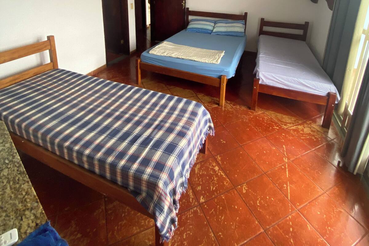 Quarto com três camas de madeira, um ventilador de teto e piso de azulejos.