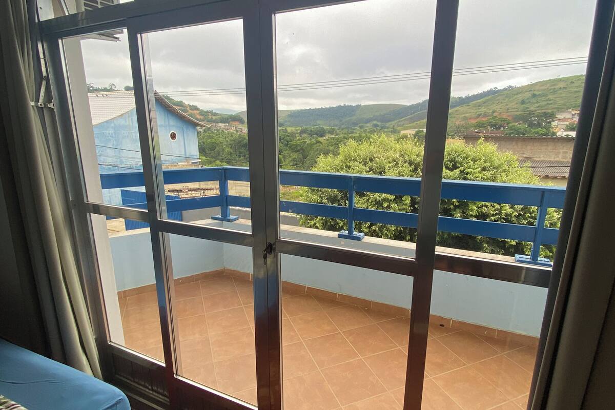 Quarto com uma janela grande dando para uma varanda com guarda-corrimão azul.