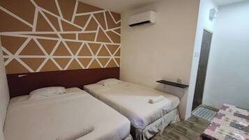 Quarto de hotel com duas camas de solteiro, ar condicionado fixado na parede, uma mesa pequena e um tapete estampado.
