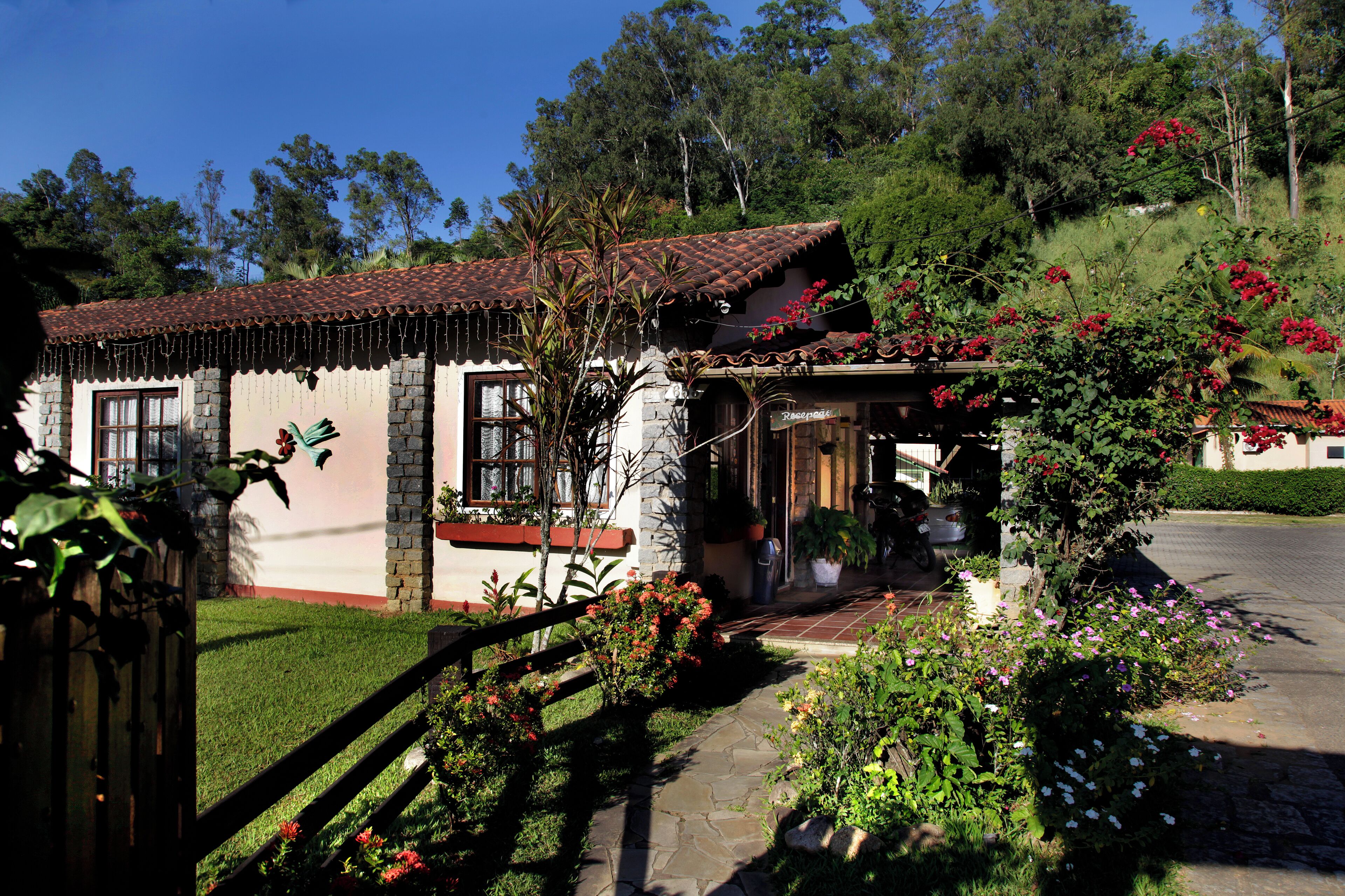 Uma pequena casa de pedra com telhado de cerâmica, rodeada por vegetação exuberante e plantas floridas.