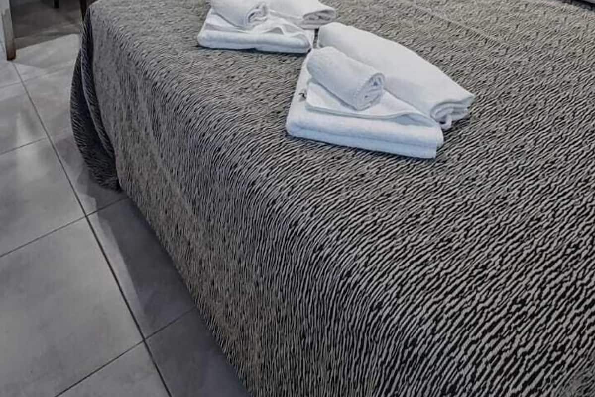 Quarto de hotel com cama grande, mesa de cabeceira, cadeira, escrivaninha e espelho.