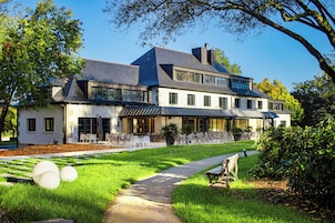 Uma casa grande de dois andares com um gramado bem cuidado, um caminho que leva à entrada e área de estar ao ar livre.
