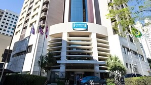 Um edifício de hotel moderno com entrada central, vários andares e varandas.