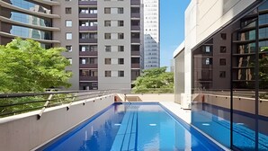 Um edifício moderno com piscina no terraço, rodeado por arranha-céus e vegetação.