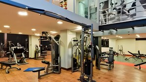 Academia com vários níveis e equipamentos de exercício, um banco azul e um espelho grande na parede.