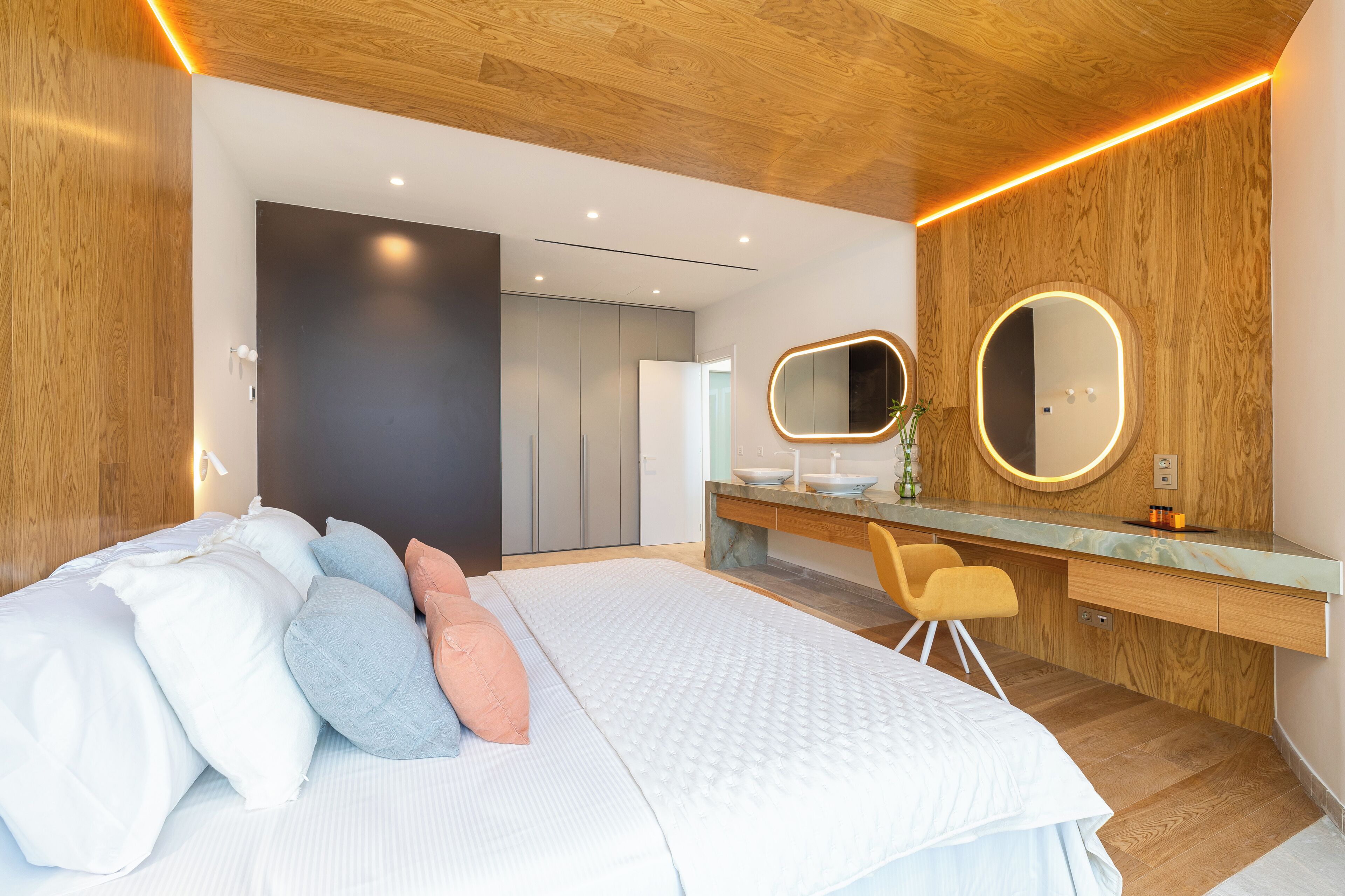 Quarto moderno com uma cama grande, uma penteadeira com espelhos e teto de madeira.