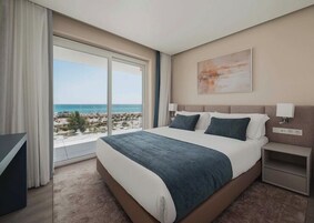 Quarto de hotel com uma cama grande, uma escrivaninha e vista para a praia.