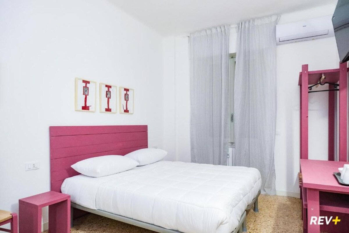 Quarto com cama, mesa de cabeceira, guarda-roupa e janela com cortinas.