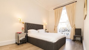 Quarto com uma cama grande, abajures, mesa de cabeceira, uma cadeira e uma janela com cortinas.