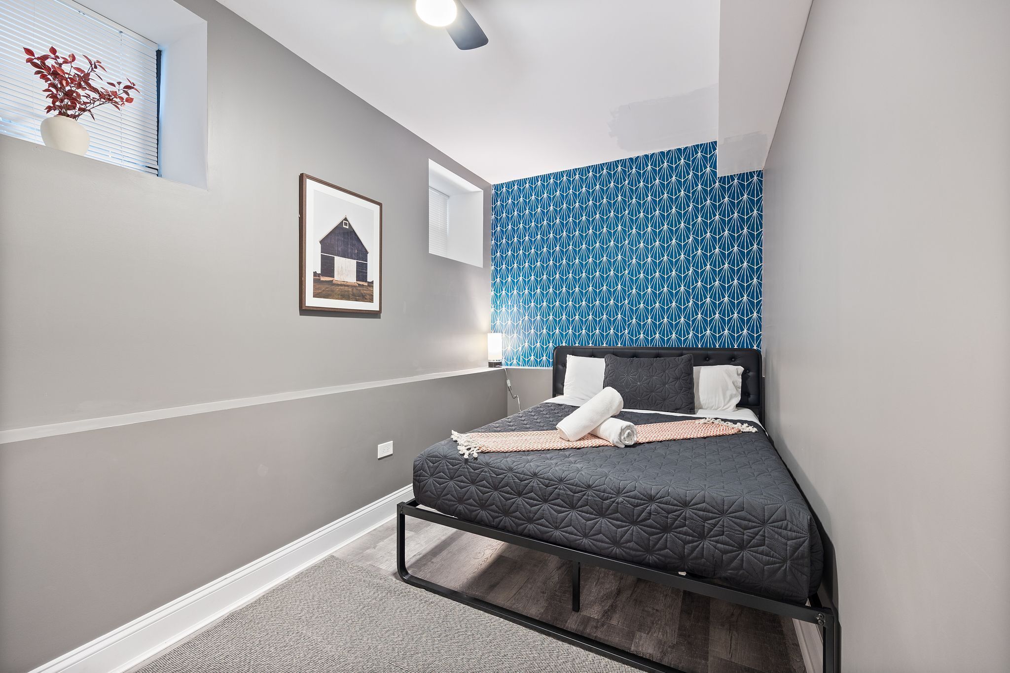 Quarto com uma cama, janela com persianas, quadro na parede e papel de parede estampado.