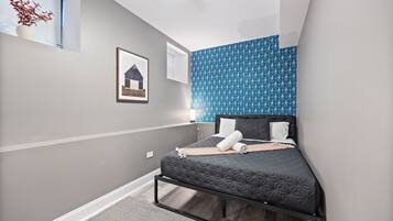Quarto com uma cama, janela com persianas, quadro na parede e papel de parede estampado.