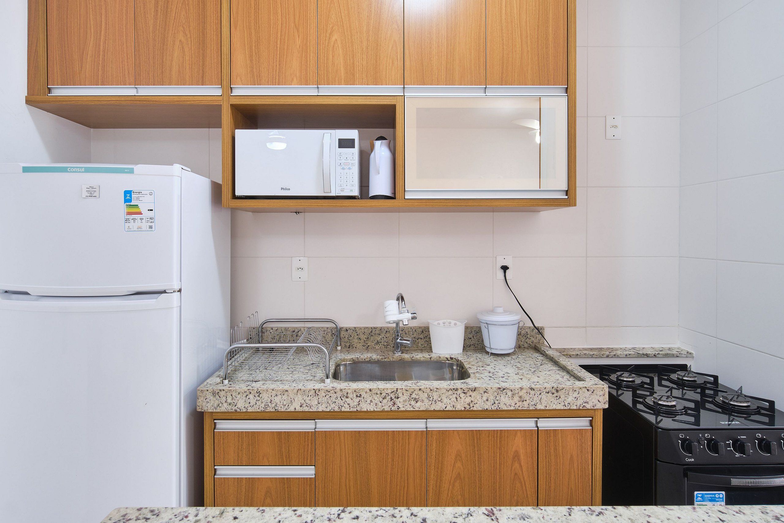 Uma cozinha com armários de madeira, geladeira branca, micro-ondas, fogão a gás e bancada de granito.