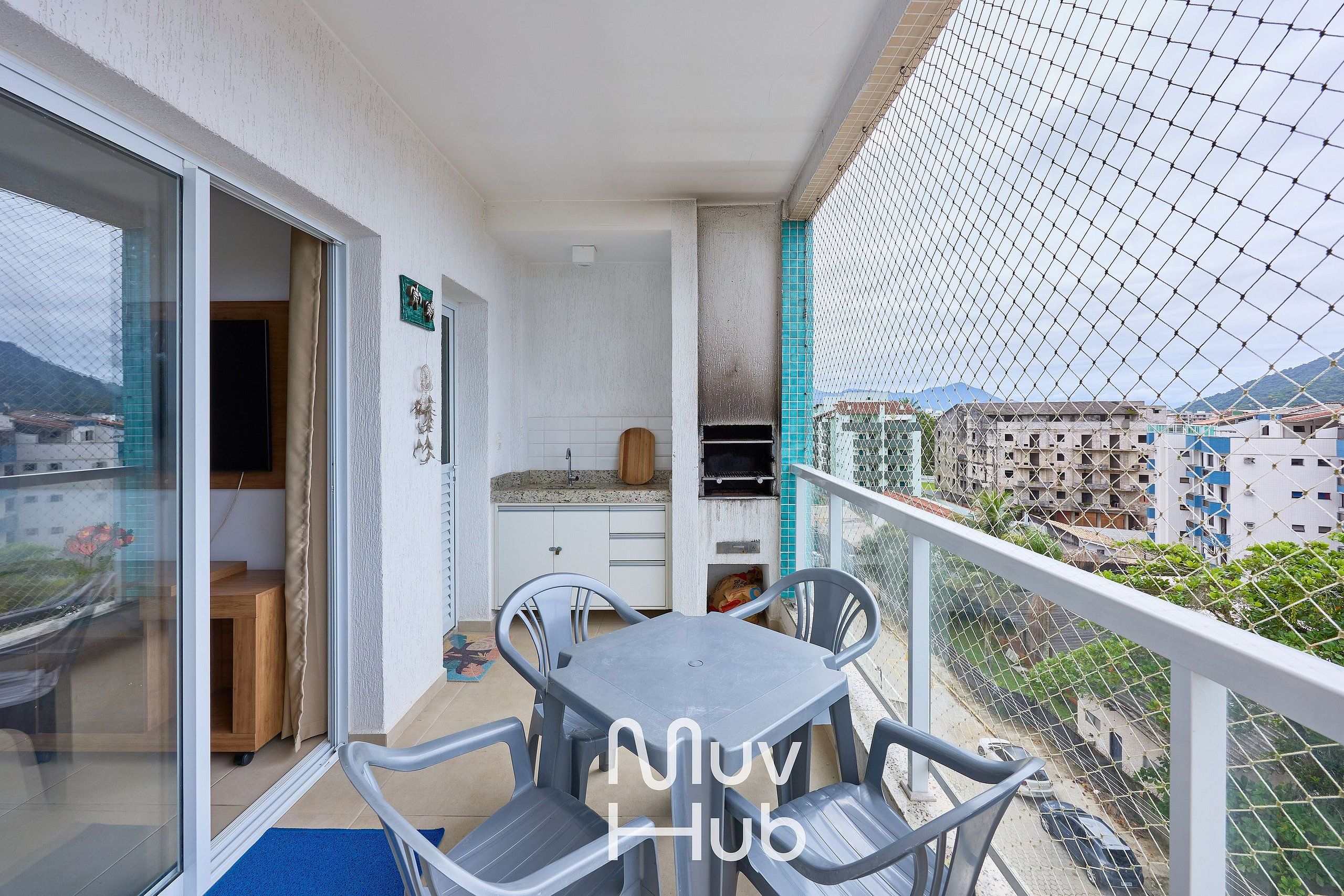 Varanda com mesa e cadeiras, porta de correr de vidro, área de cozinha e vista para a cidade.