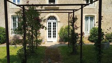 Um caminho coberto por um jardim que leva a um edifício com entrada de pedra e janelas em arco.