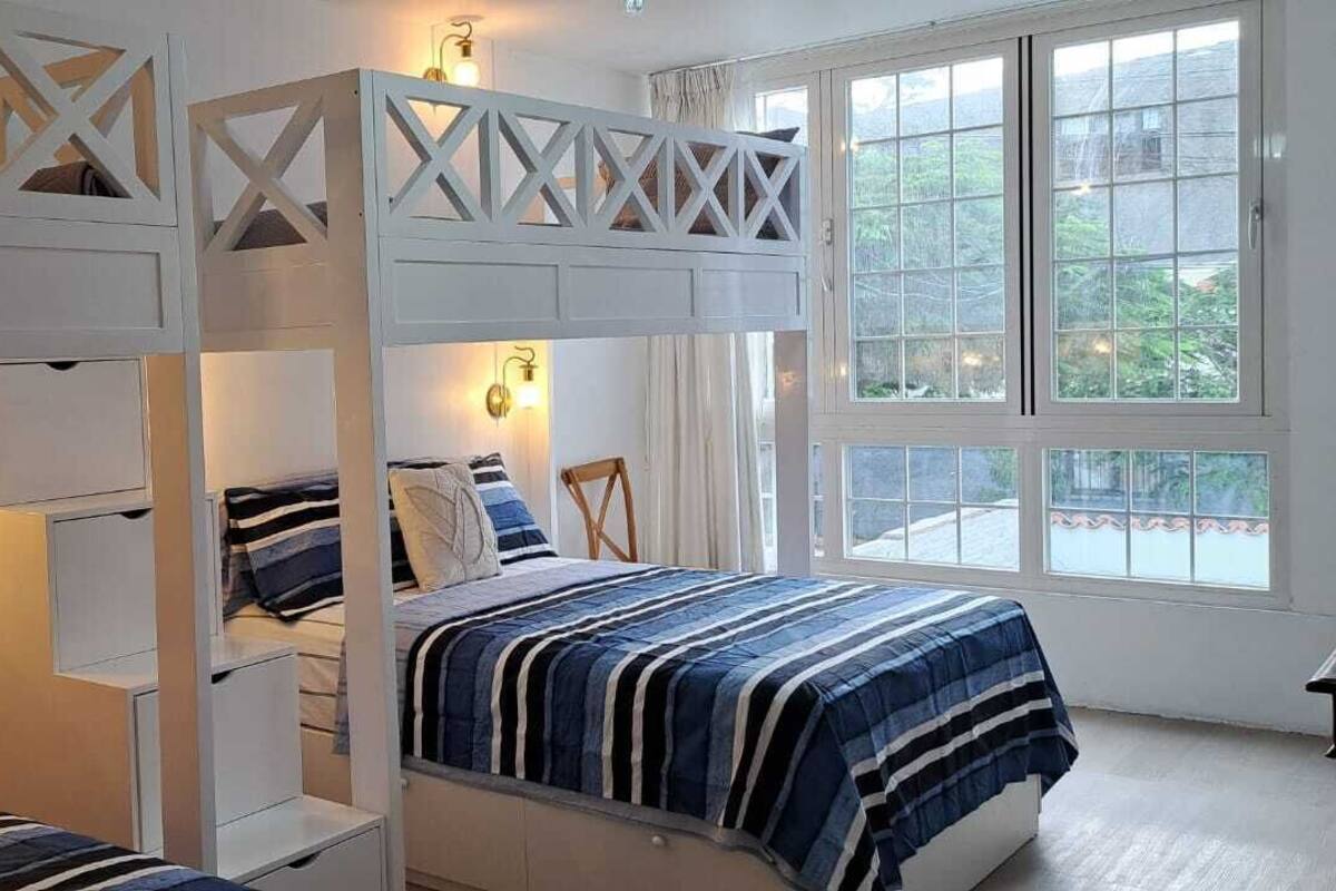 Quarto com beliches, janela com cortinas e luminárias fixadas na parede.