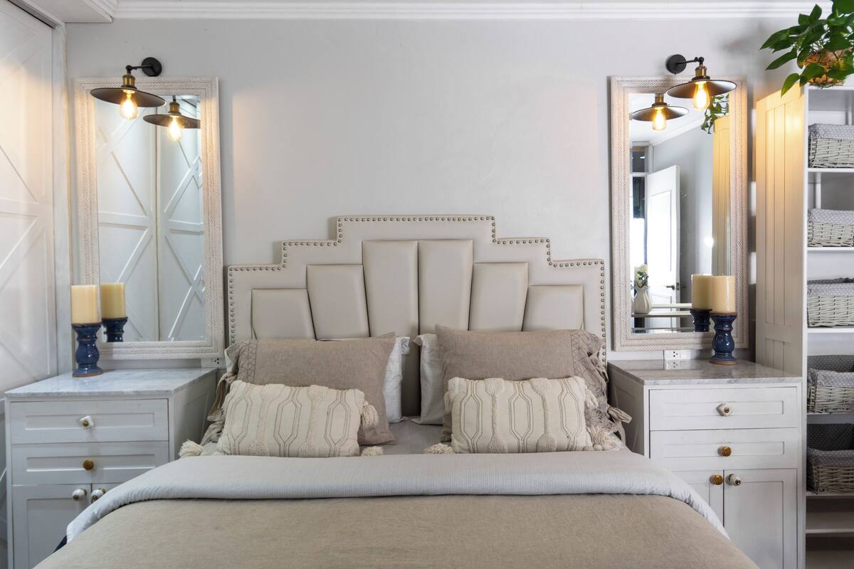 Quarto com cama grande, duas mesas de cabeceira, cômoda e duas luminárias fixadas na parede.