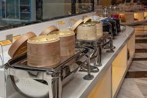 Disposição de buffet com diversos recipientes de comida e um espaço para bebidas.
