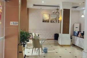 Um saguão de hotel com balcão de recepção, área de estar com cadeiras, uma lixeira e um vaso de planta.