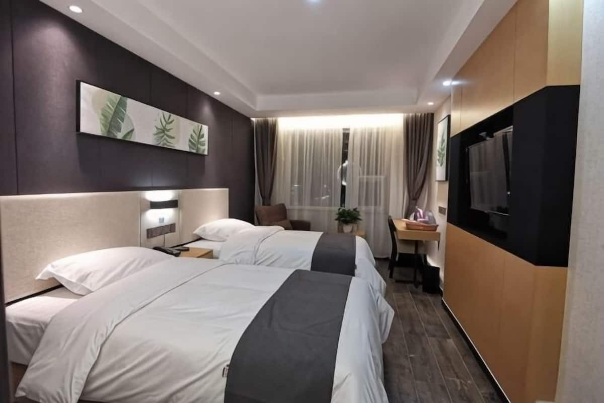 Quarto de hotel com duas camas, uma escrivaninha, uma televisão e uma janela com cortinas.
