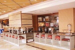 Uma área de buffet com vários pontos de serviço, espaço para sentar e um bar com diversos itens expostos.
