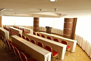 Uma sala de conferência com fileiras de cadeiras, um púlpito e piso coberto de carpete.