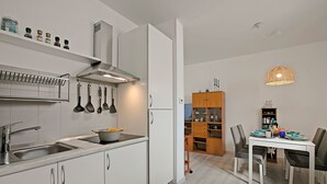 Uma cozinha moderna com armários brancos, uma pia de aço inoxidável e uma área de jantar com mesa e cadeiras.