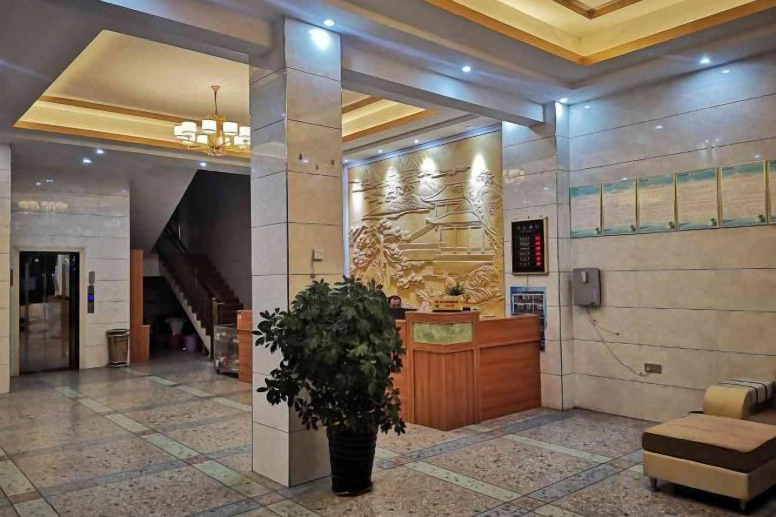 Um hall de hotel com balcão de recepção, escadaria e planta em vaso.