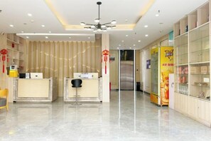 Uma área de recepção de hotel com design moderno, incluindo um balcão de atendimento, um espaço de estar e uma máquina de vendas automática.