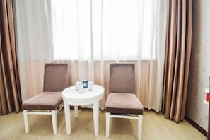 Quarto com duas cadeiras e uma pequena mesa redonda, cortinas e uma janela.