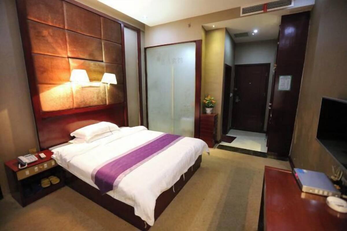 Quarto de hotel com cama, mesa de cabeceira, luminária, guarda-roupa e televisão.