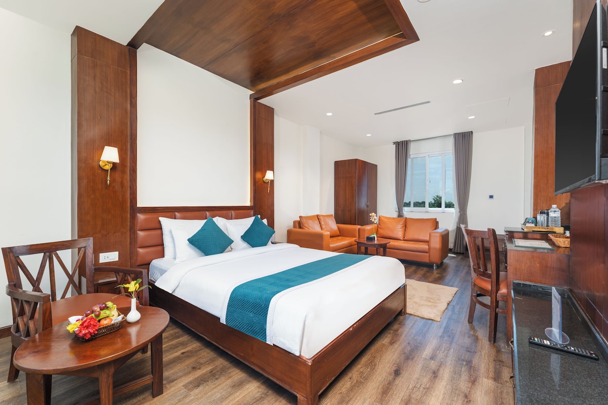 Quarto de hotel com uma cama grande, escrivaninha, cadeira, sofá e televisão.