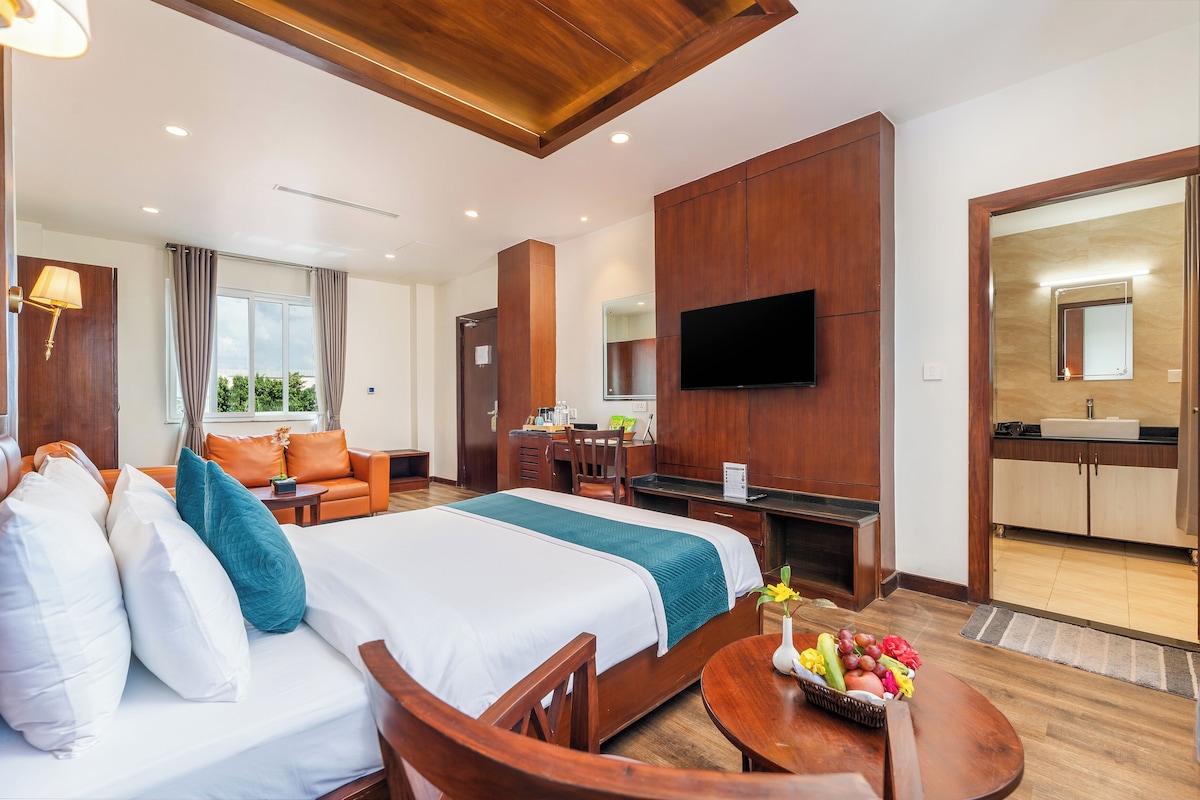 Quarto de hotel com cama, escrivaninha, televisão e banheiro.