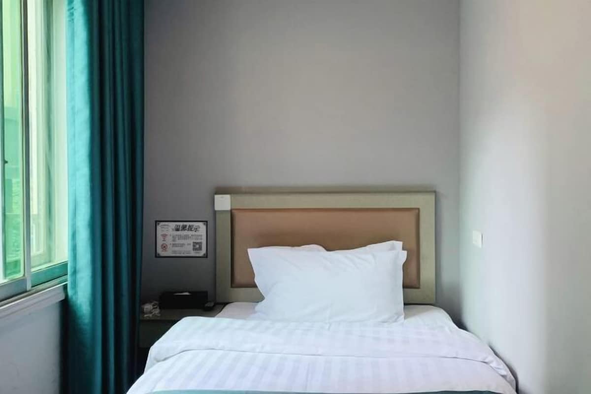 Uma cama pequena e bem arrumada com cabeceira de madeira em quarto com janela e placa fixada na parede.