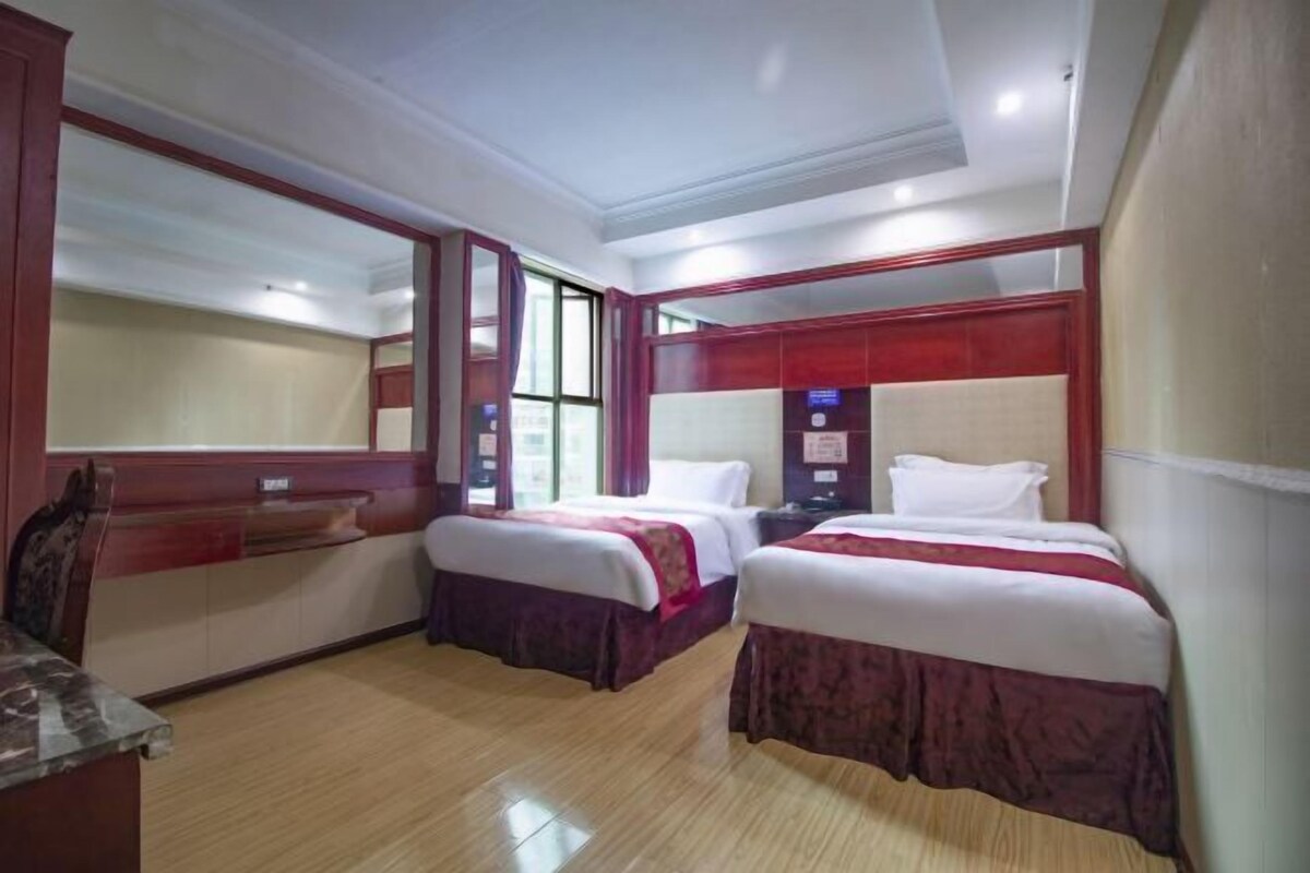 Quarto de hotel com duas camas, piso de madeira e um espelho grande em uma das paredes.