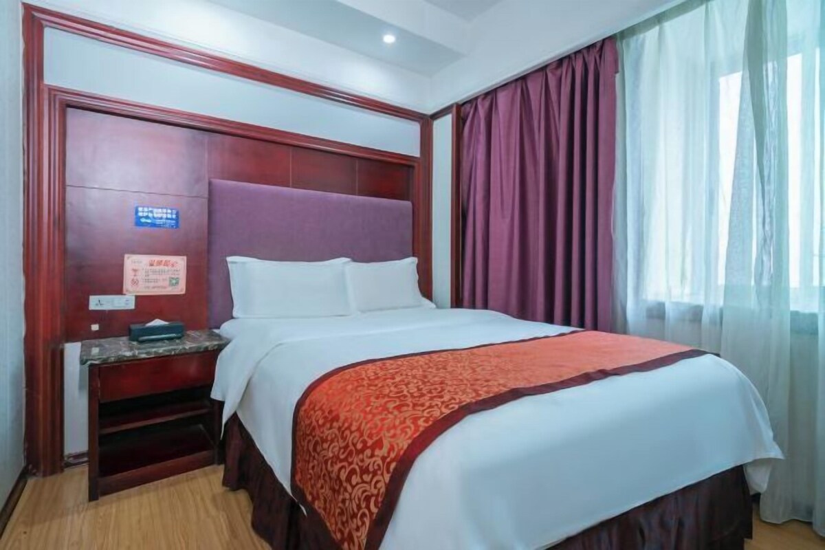 Quarto de hotel com uma cama grande, cabeceira de madeira, mesa de cabeceira e uma janela com cortinas.