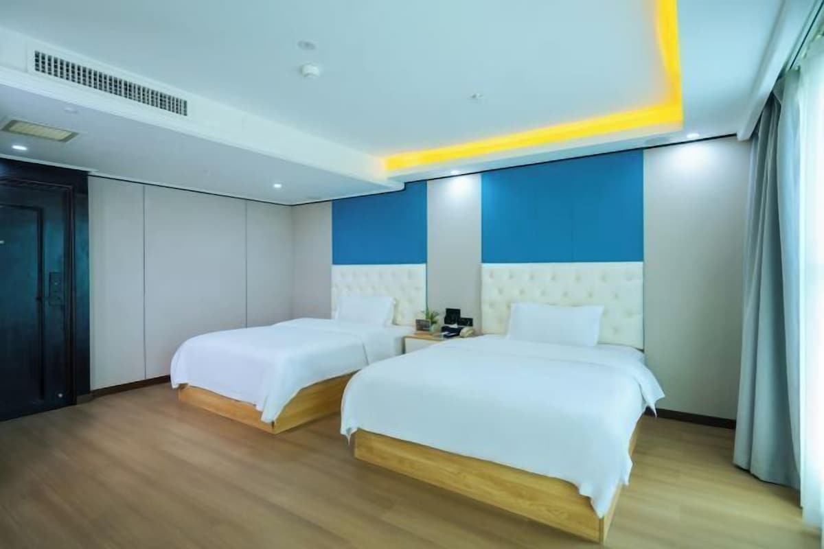 Quarto de hotel com duas camas, piso de madeira, parede azul e design moderno.