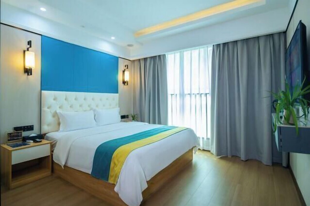 Quarto de hotel moderno com uma cama grande, mesa de cabeceira, televisão na parede e janela com cortinas.