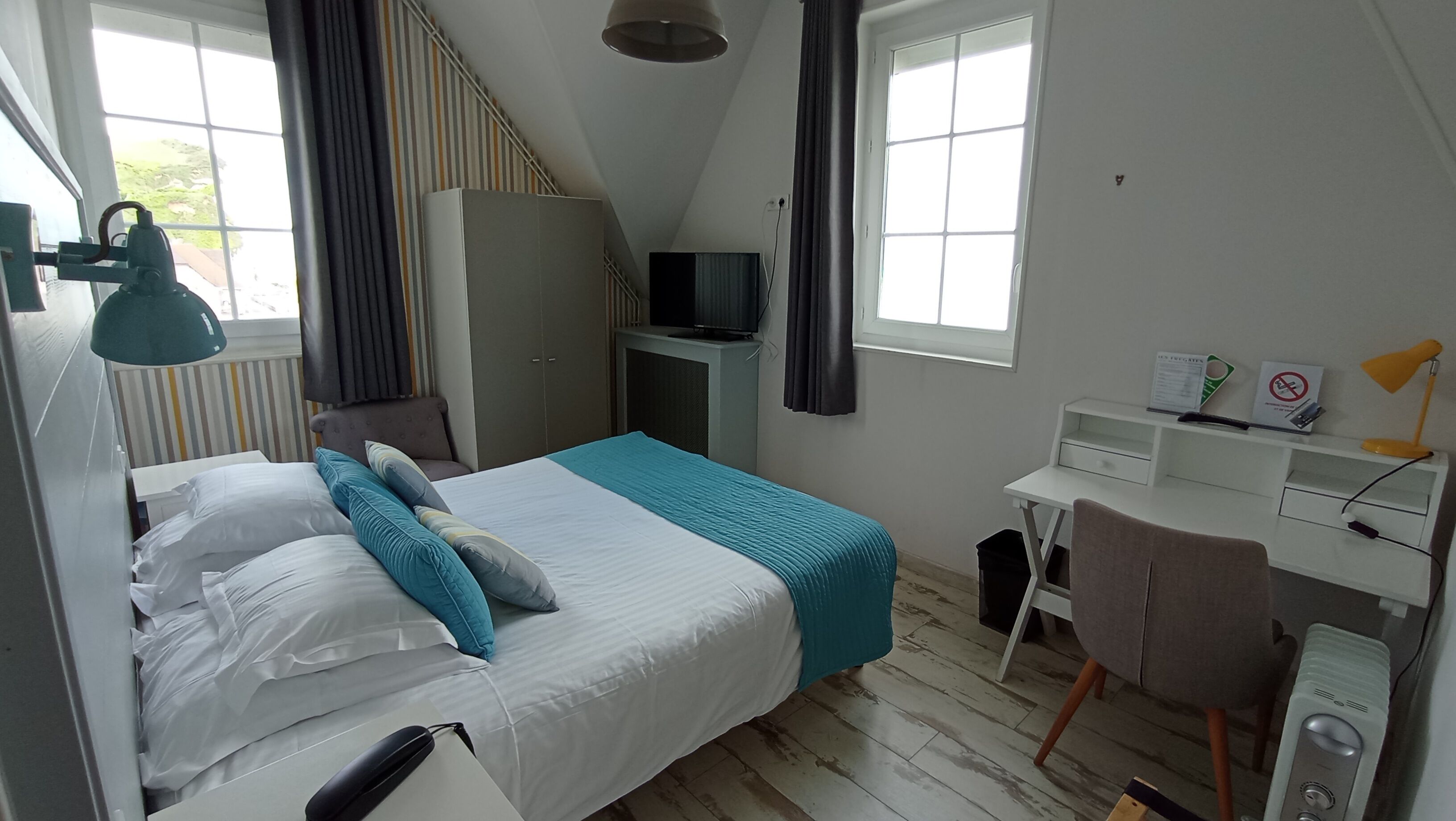 Quarto com cama, escrivaninha, cadeira, televisão e janela.