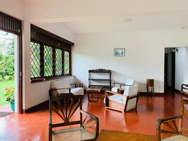Um quarto espaçoso com piso de madeira, uma grande janela com padrão de treliça e uma área de estar com dois sofás e duas cadeiras.