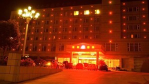 Um hotel com vários andares, entrada central e estacionamento com diversos carros.