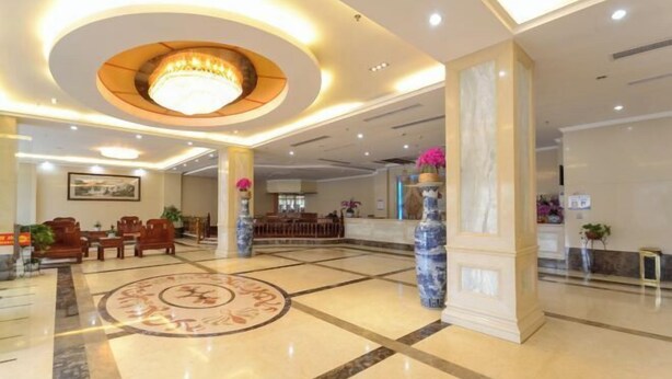 Um hall amplo com um lustre central, piso de mármore e um balcão de recepção.