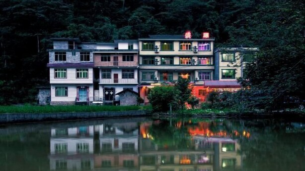 Edifício de vários andares com varandas, reflexo na água e entrada iluminada em vermelho.