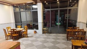 Um espaço amplo e interno com piso xadrez, mesas e cadeiras de madeira, e grandes janelas que proporcionam iluminação natural.