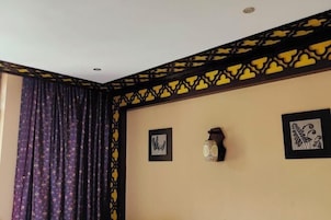 Um quarto com cortina estampada, parede com borda decorativa preta e amarela, e duas molduras.