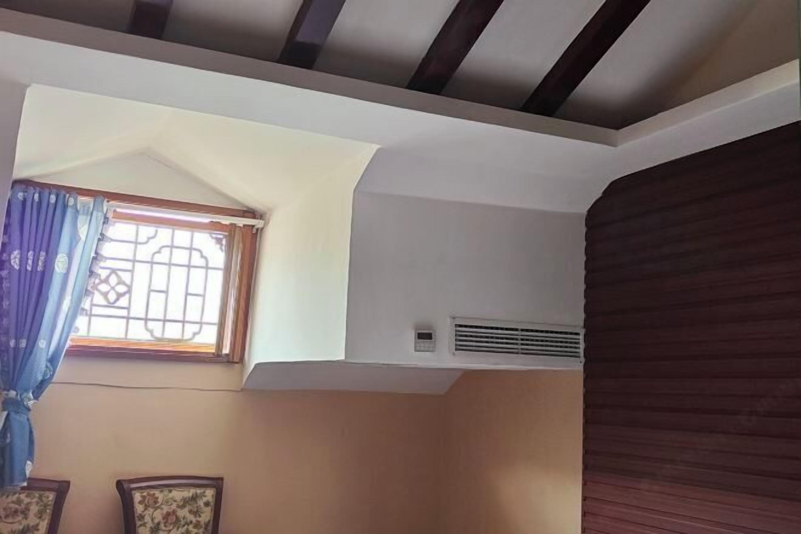 Um quarto com teto inclinado, janela com grade de metal, ar condicionado e duas cadeiras com padrão floral.