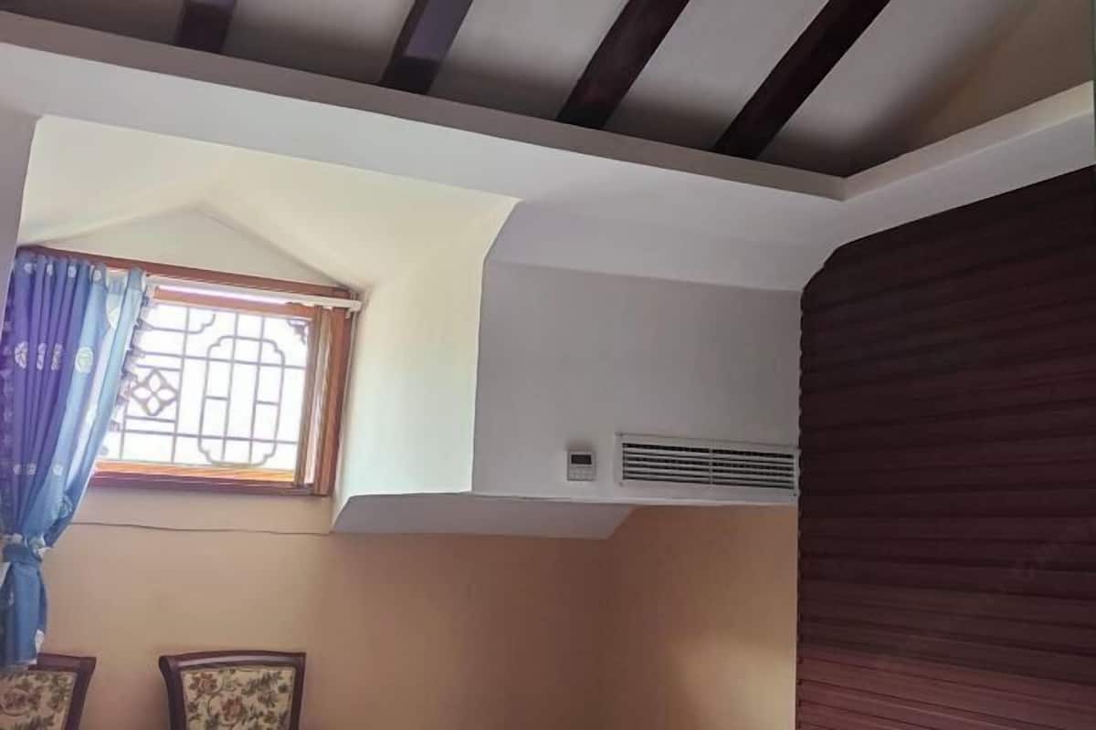 Um quarto com teto inclinado, janela com grade de metal, ar condicionado e duas cadeiras com padrão floral.