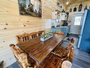 Uma mesa de jantar de madeira com cadeiras, uma área de cozinha com armários e um lustre.