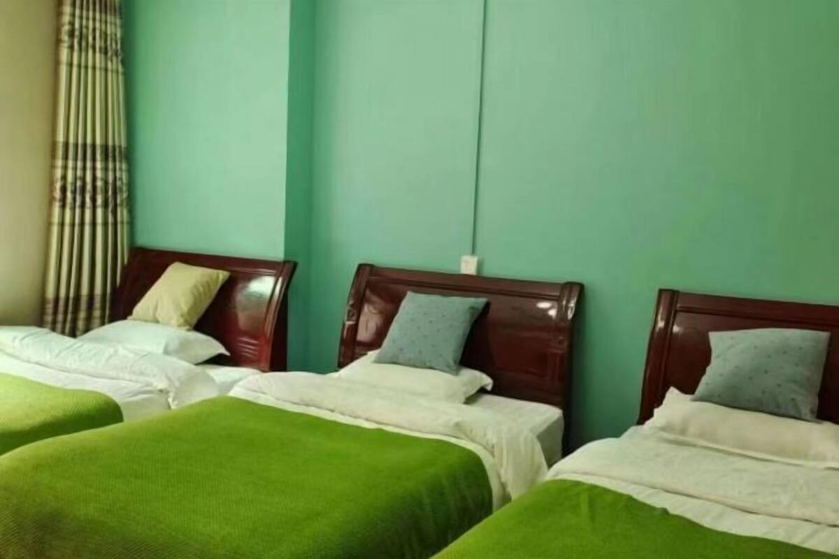 Quarto de hotel com três camas, cada uma com cabeceira de madeira e roupa de cama verde.