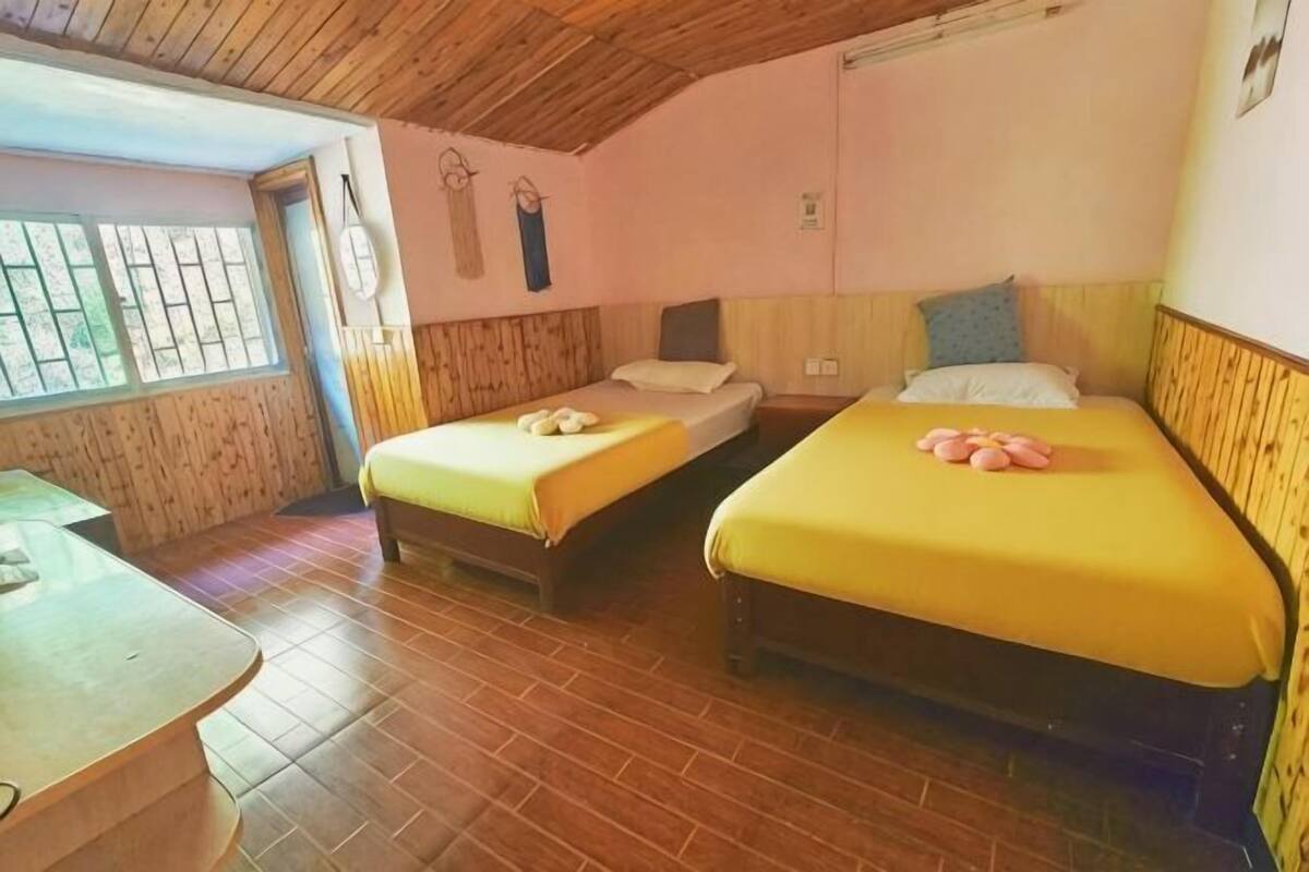 Quarto com duas camas, teto de madeira e janela com grades.